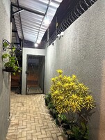 Um caminho de tijolos estreito que leva a um portão, cercado por paredes texturizadas e vasos de plantas.