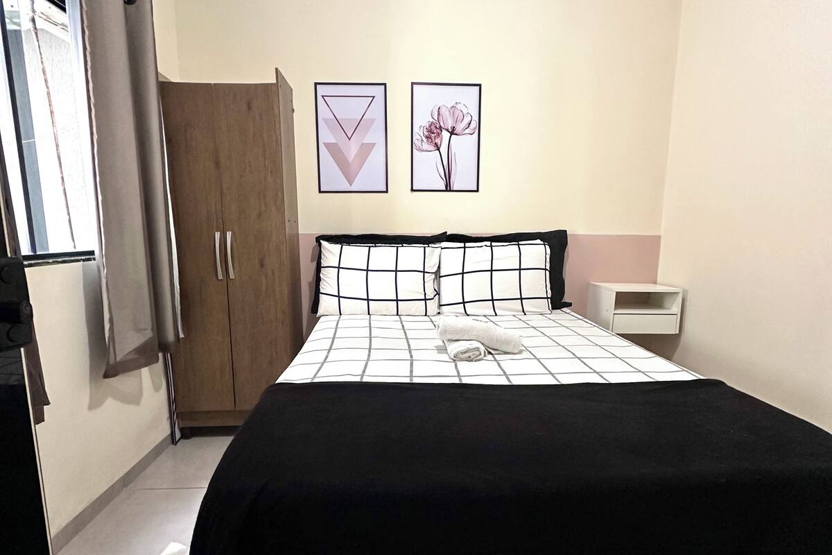 Quarto com cama, guarda-roupa, mesa de cabeceira e duas fotografias emolduradas na parede.
