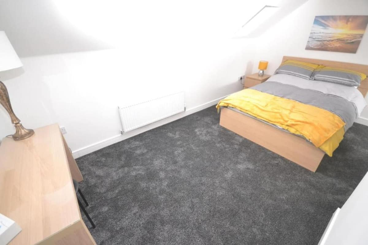 Quarto com cama, mesa de cabeceira, abajur e um quadro na parede.