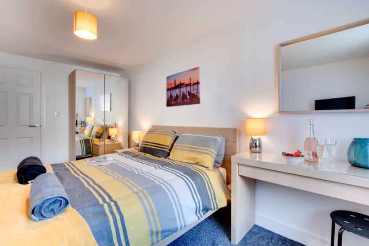 Quarto de hotel com cama, mesa de cabeceira, luminária e um quadro na parede.
