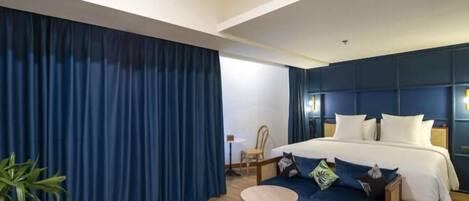 Quarto de hotel moderno com uma cama grande, um sofá, uma mesinha redonda e um vaso de planta.