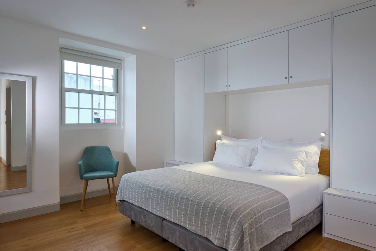 Quarto com cama, cadeira, guarda-roupa e janela.