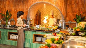 Disposição de buffet com um chef cozinhando ao fundo, rodeado por diversos alimentos e utensílios de buffet.