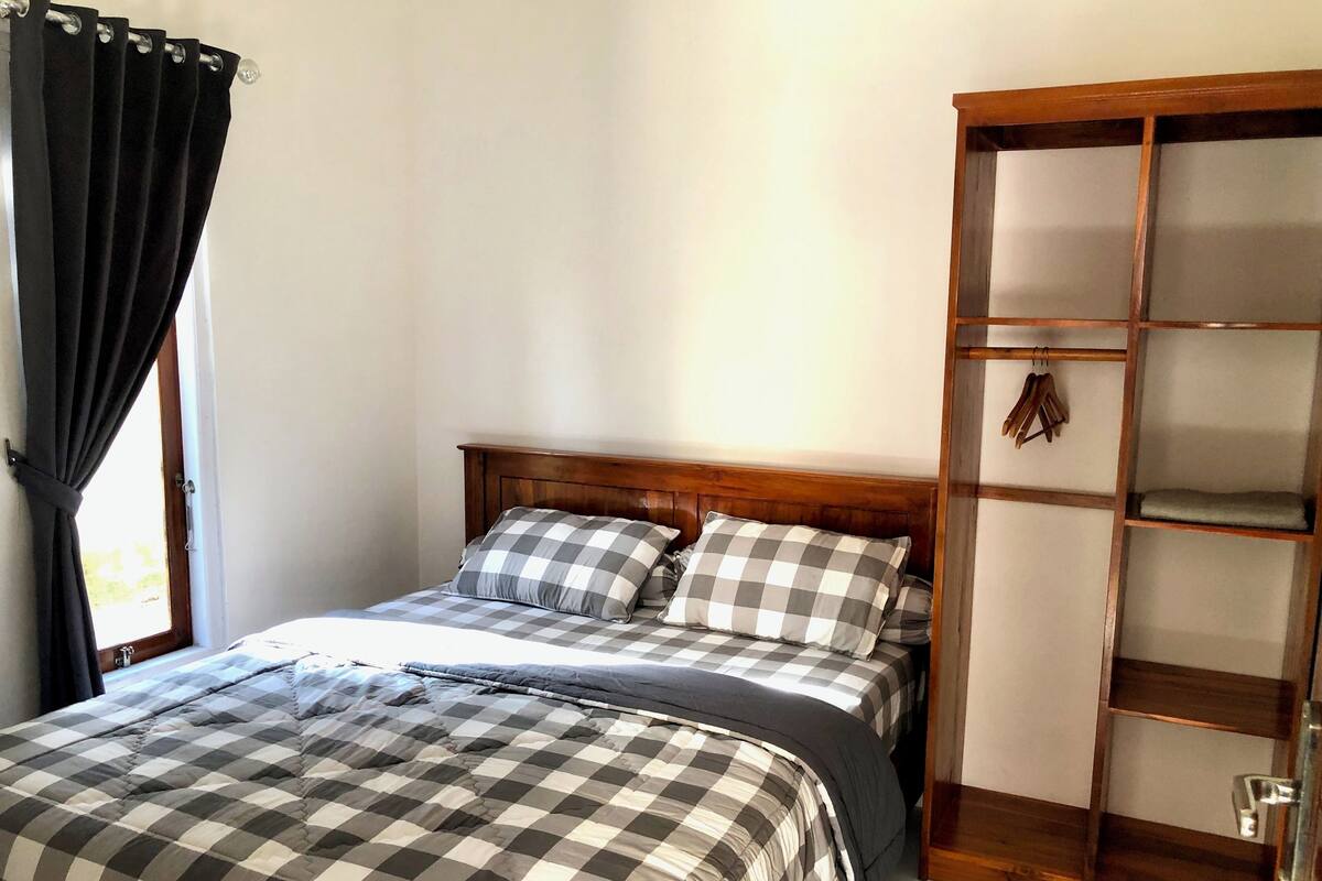 Quarto com colcha xadrez, cabeceira de madeira e armário embutido com prateleiras.