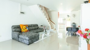 Uma sala de estar moderna com um sofá seccional cinza, uma mesa de centro de vidro e uma escada que leva a outro andar.
