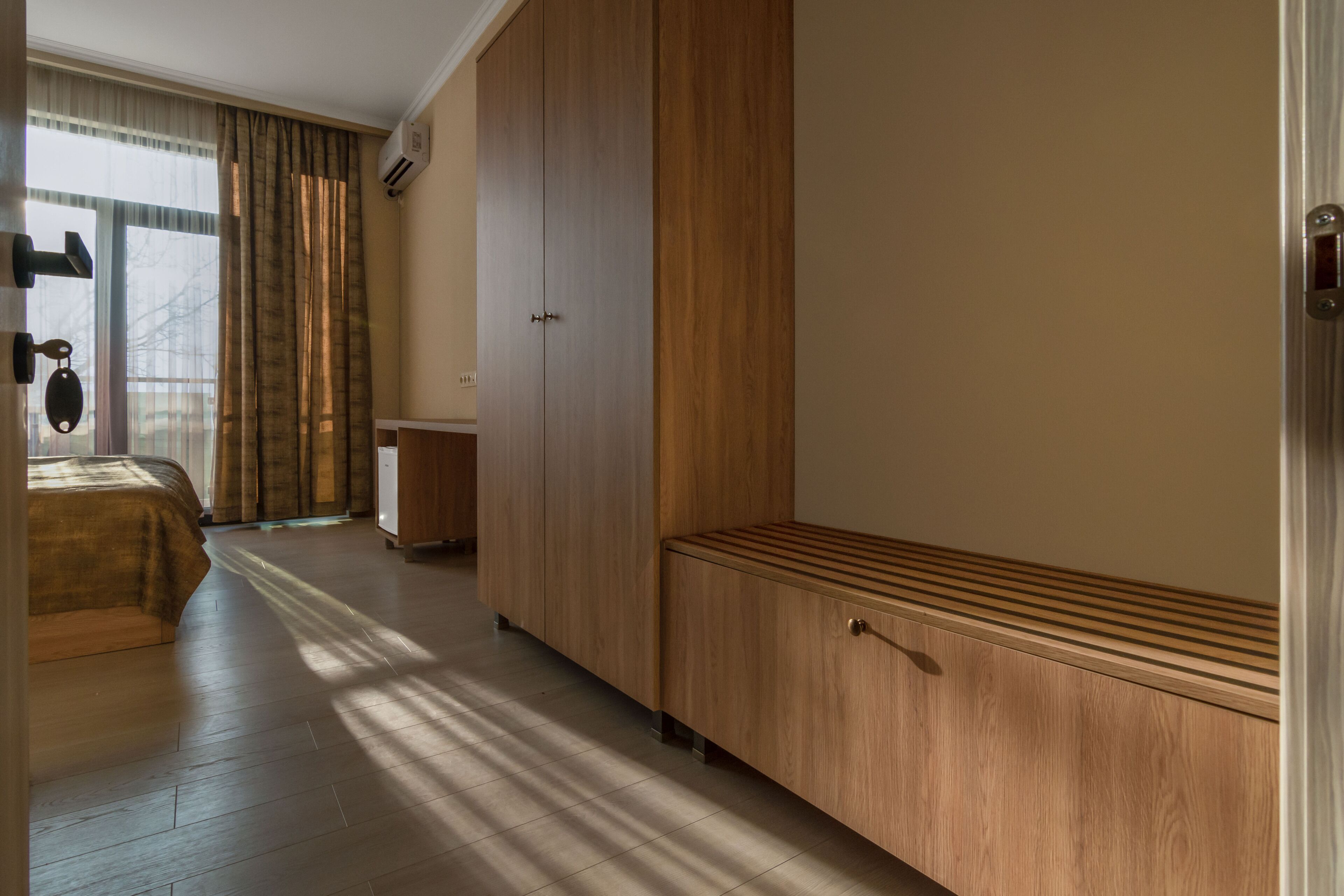 Quarto de hotel com um guarda-roupa grande, uma cama e um banco.