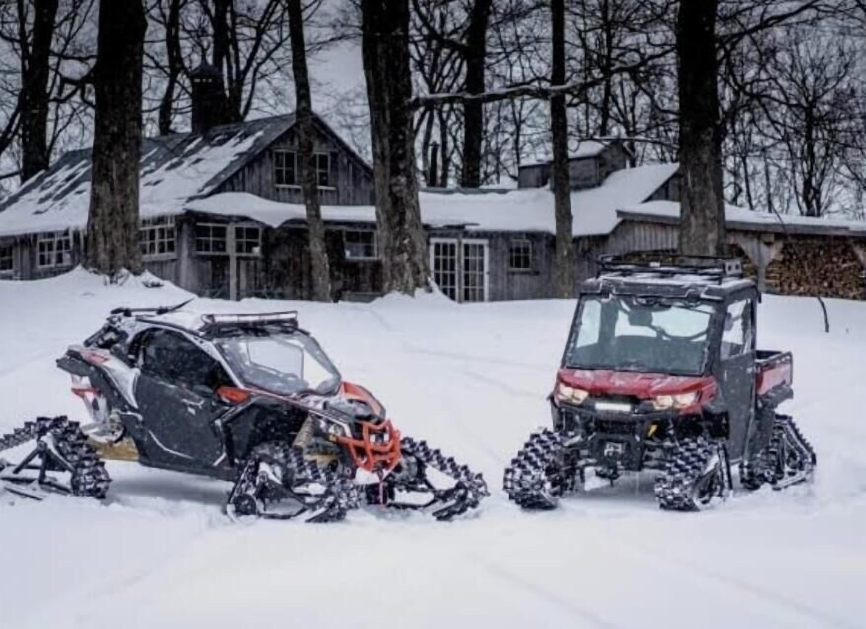 Duas motos de neve em uma paisagem nevada, com uma casa ao fundo.