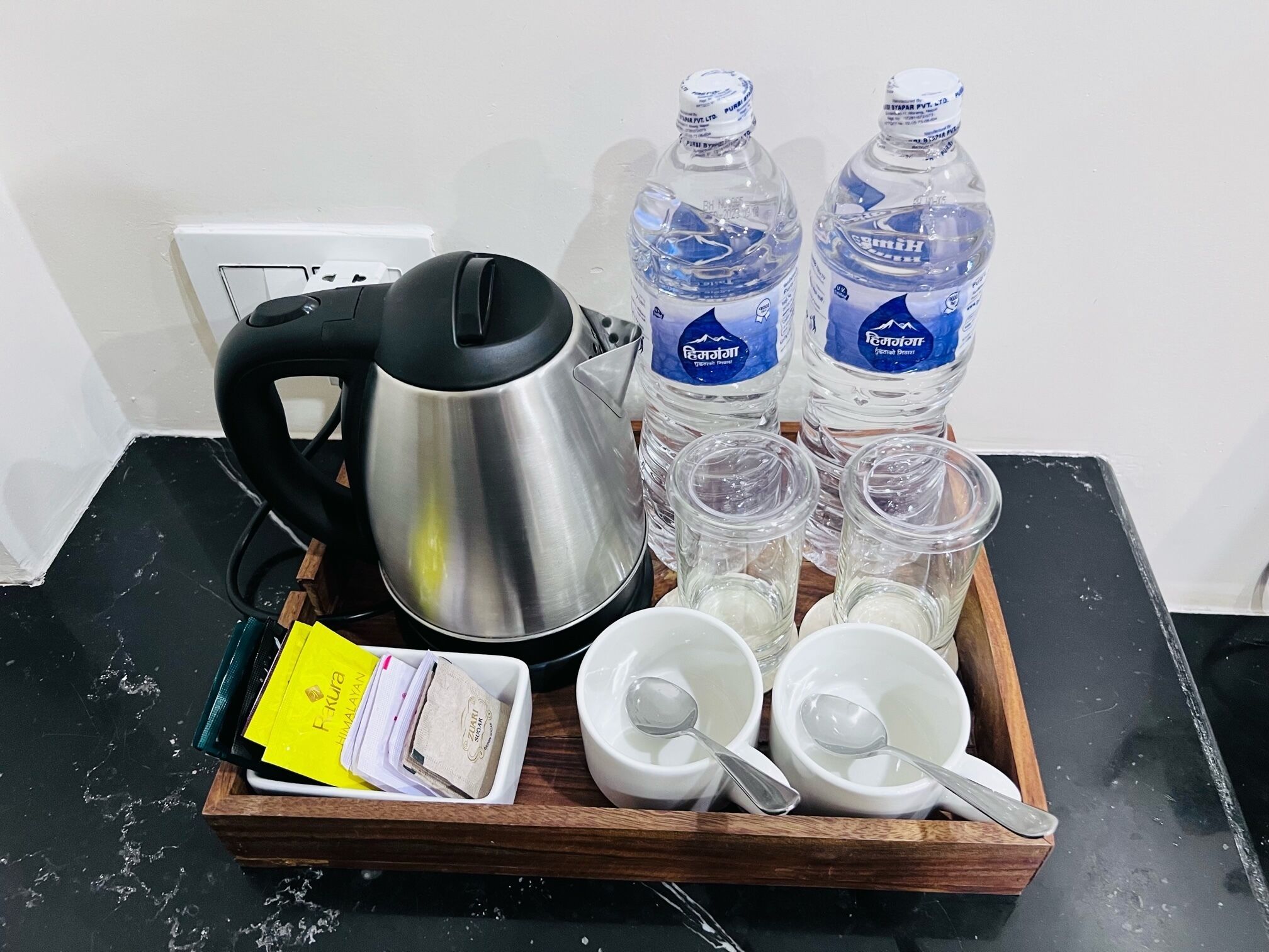 Uma bandeja com chaleira, garrafas de água, xícaras, colheres e um pequeno recipiente com cartas.