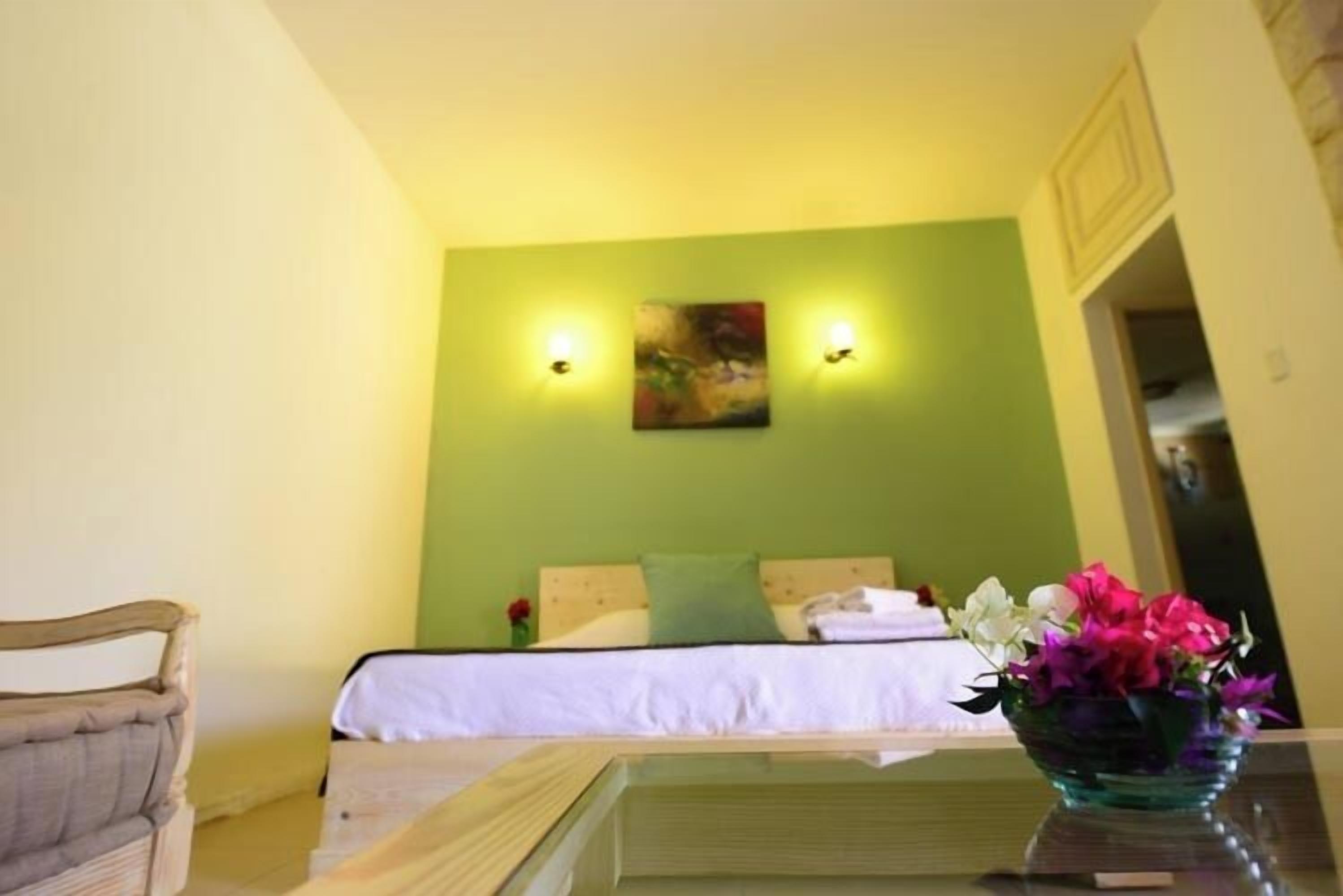 Quarto de hotel com uma cama, uma mesinha com um vaso de flores e duas luminárias na parede.