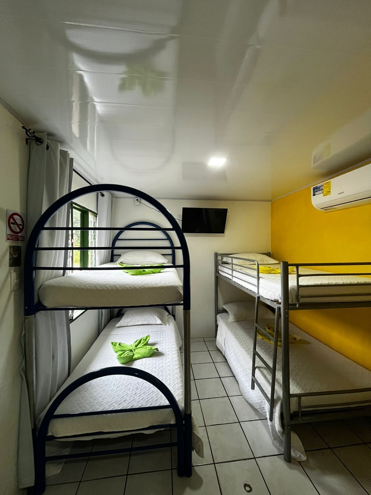 Quarto com beliche, televisão na parede e janela com cortinas.