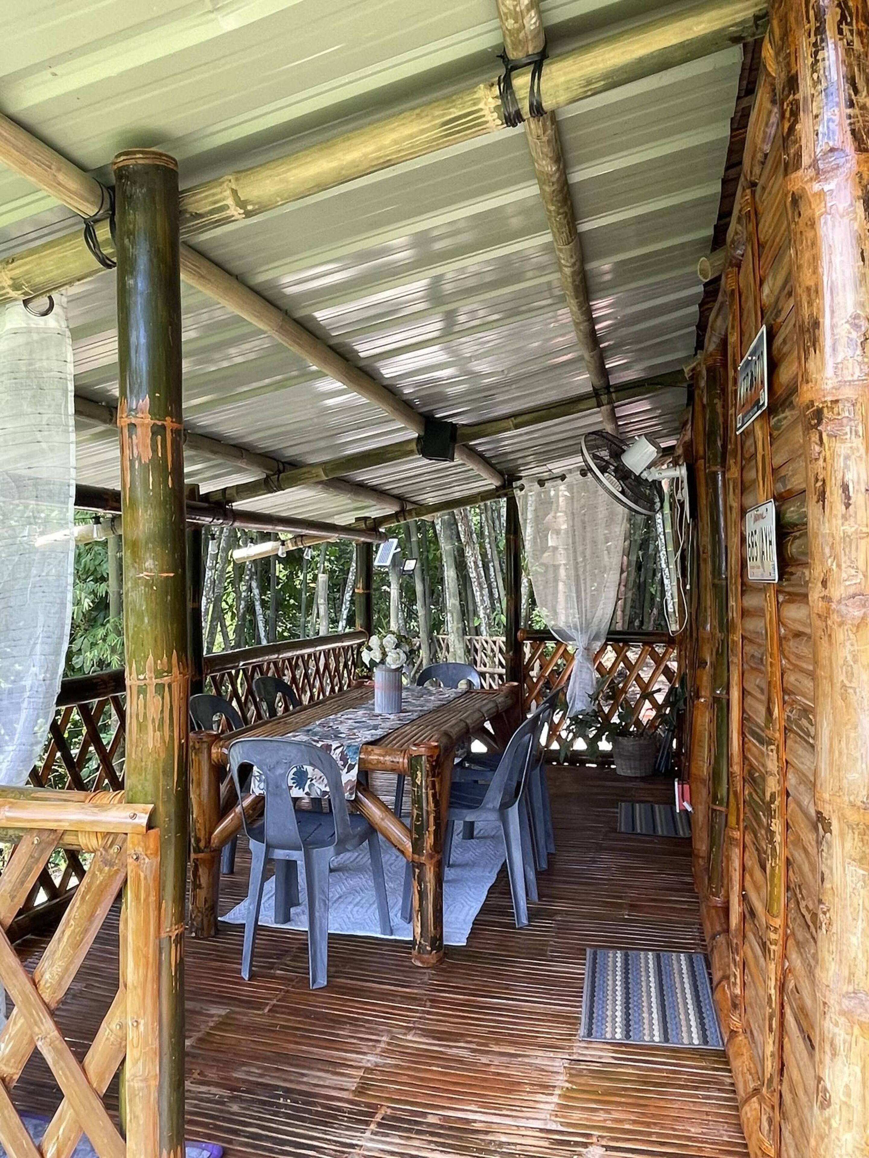 Uma área de refeições ao ar livre coberta, com mobiliário de bambu e teto de metal.
