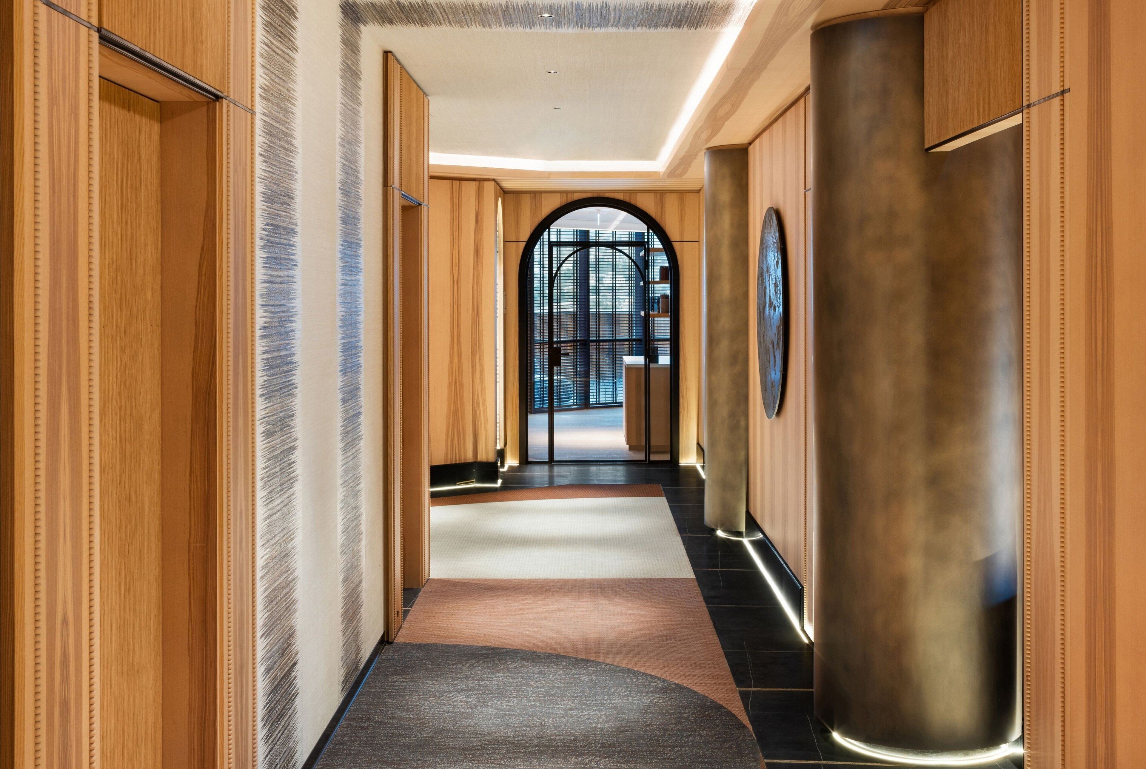 Corredor moderno de hotel com painéis de madeira, parede estampada em preto e branco e uma grande obra de arte circular.