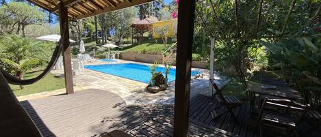 Um deck de madeira com piscina, móveis de exterior e uma rede.