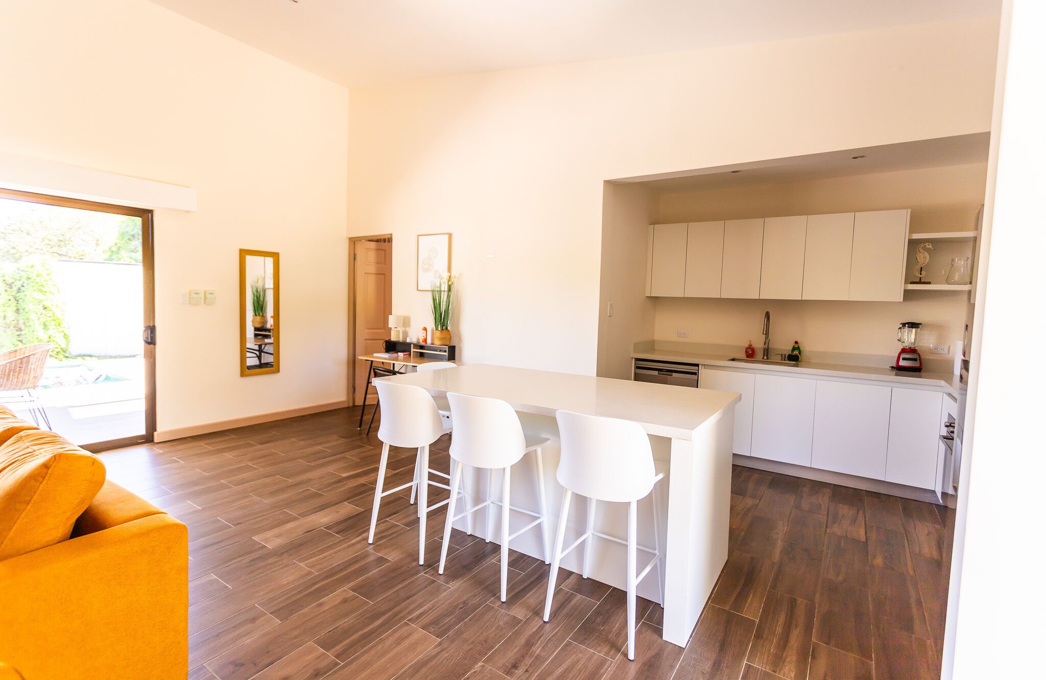 Uma cozinha moderna com armários brancos, um espaço bar com banquetas brancas e uma mesa de jantar.
