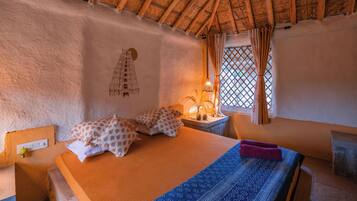 Quarto com uma cama, mesa de cabeceira, luminária na parede e janela com treliça.