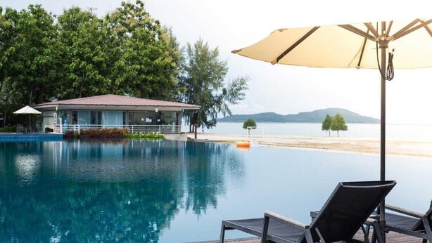 Piscina com espreguiçadeiras e guarda-sol, cercada por árvores e vista para a costa distante.
