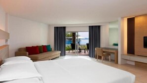 Quarto de hotel com cama, sofá com almofadas coloridas, escrivaninha e televisão.