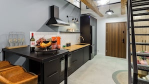 Cozinha moderna com armários pretos, bancada de madeira e forno embutido. Há uma cadeira de madeira e uma fruteira sobre a bancada.
