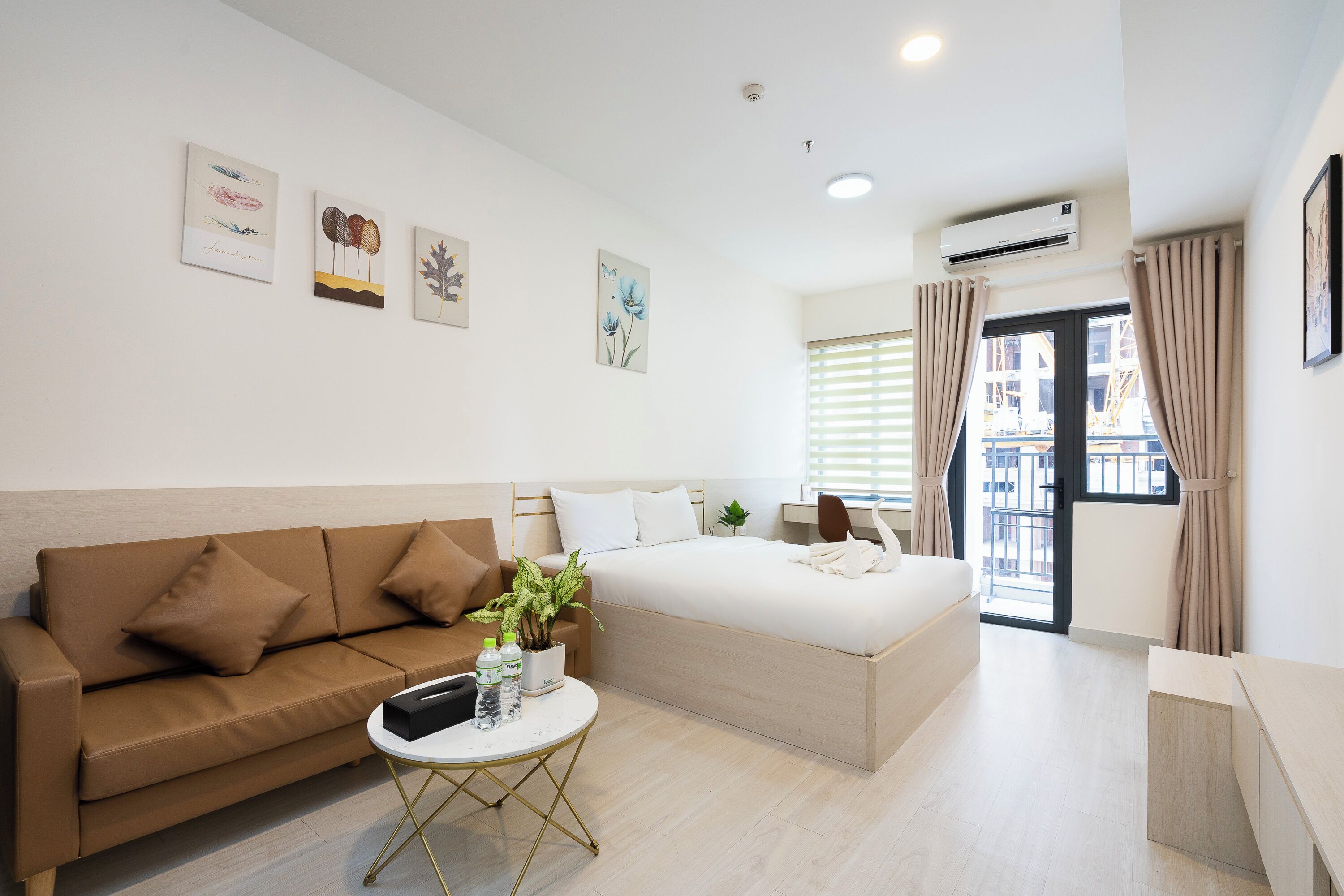 Quarto de hotel moderno com sofá, cama, mesinha redonda com garrafas de água e obras de arte nas paredes.
