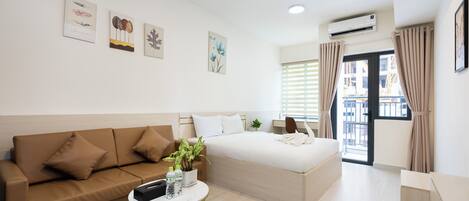 Quarto de hotel moderno com sofá, cama, mesinha redonda com garrafas de água e obras de arte nas paredes.