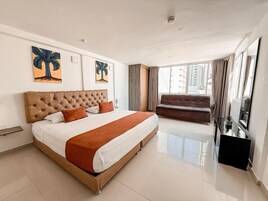 Quarto de hotel com uma cama grande, um sofá, uma TV e uma varanda com cortinas.