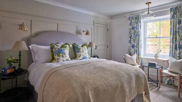Quarto com uma cama grande, duas luminárias de cabeceira, uma mesa de cabeceira com um rádio, uma cadeira perto da janela e vista para o jardim.
