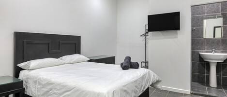 Quarto moderno com uma cama grande, mesa de cabeceira, televisão na parede e banheiro com pia e espelho.