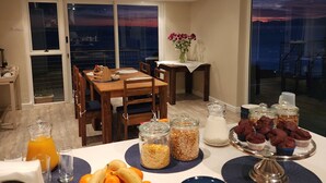 Uma sala de jantar com uma mesa posta para o café da manhã, incluindo frutas, cereais e doces.