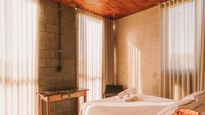 Quarto com cama, mesa de cabeceira, abajur e parede de tijolos.