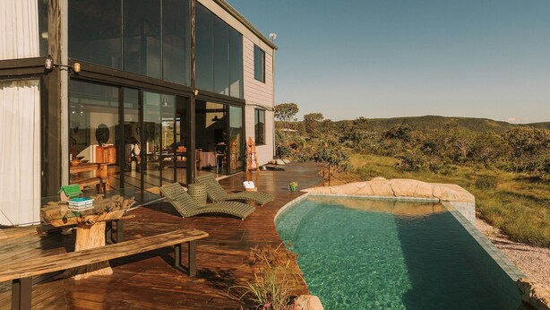 Uma casa moderna com uma grande janela de vidro, um deck de madeira e uma piscina.
