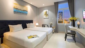 Quarto de hotel com duas camas, uma escrivaninha, uma cadeira, uma janela com vista para a cidade e obras de arte nas paredes.