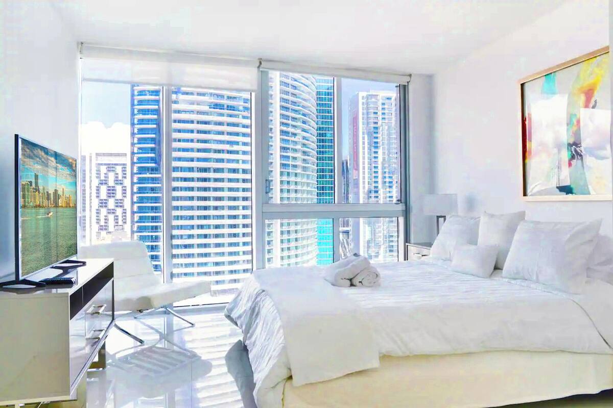 Quarto de hotel moderno com uma cama grande, uma escrivaninha, uma cadeira e uma televisão.