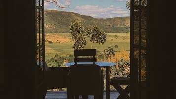 Pátio aberto com mesa e cadeiras, com vista para uma paisagem montanhosa sob céu claro.