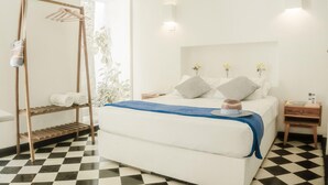 Quarto com piso xadrez, cama com manta azul, um varal de madeira e uma mesa de cabeceira com abajur.