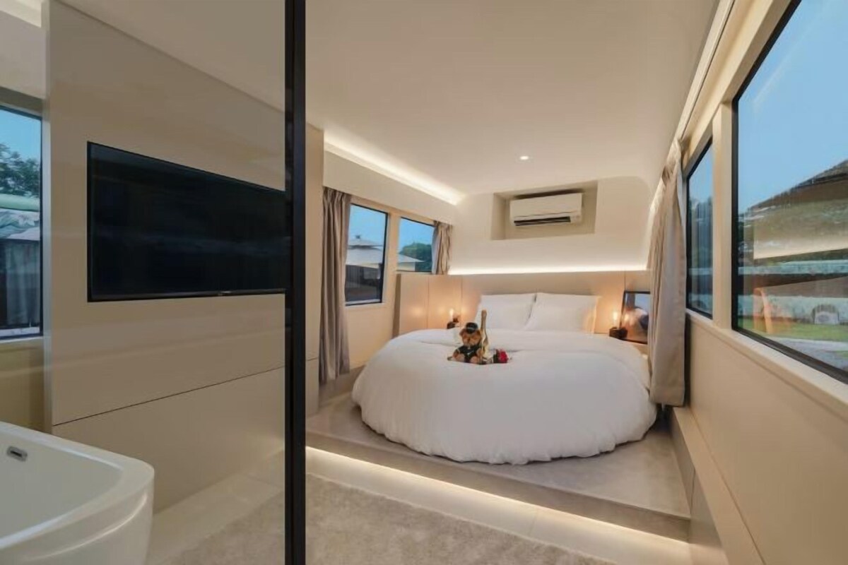 Quarto moderno com cama grande, televisão na parede e janela com vista para o exterior.