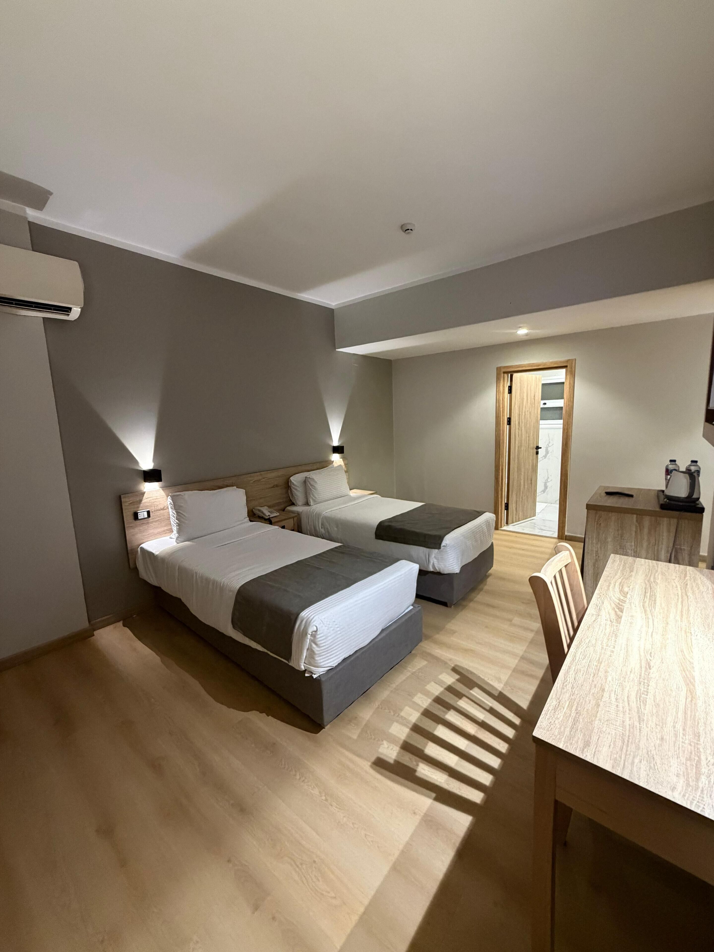 Quarto de hotel com duas camas, uma mesa de madeira e uma escrivaninha com uma cadeira.