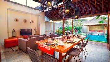 Ampla sala de estar com mesa de jantar posta para refeição, área de estar confortável e vista para uma piscina.