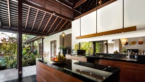 Cozinha moderna com uma ilha grande, armários de madeira e vista para um jardim tropical.