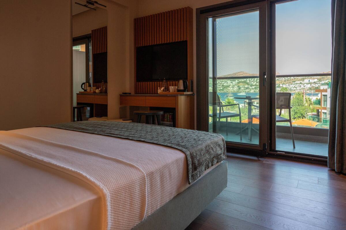 Quarto de hotel com cama, televisão, escrivaninha com cadeira e varanda com vista.