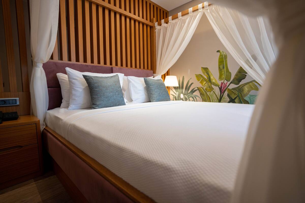 Uma cama bem arrumada com roupa de cama branca, uma cabeceira de madeira e uma mesa de cabeceira com abajur.