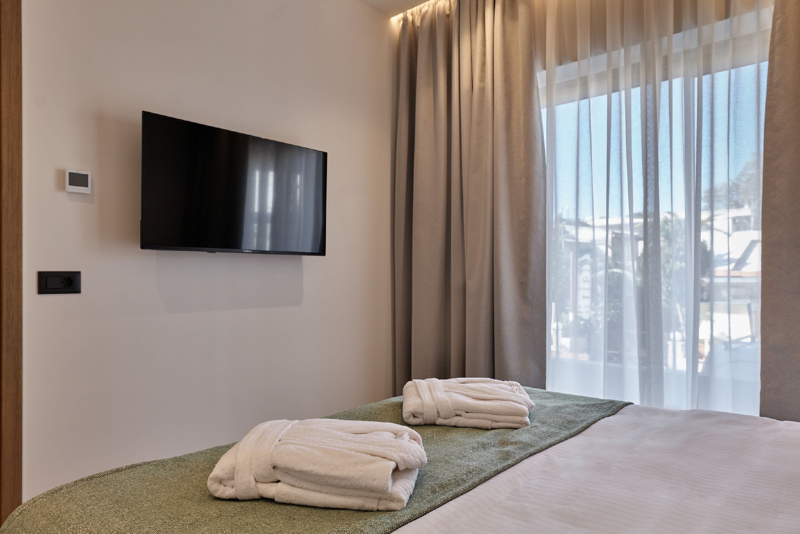 Quarto de hotel com cama, TV de tela plana fixada na parede e janela com cortinas.