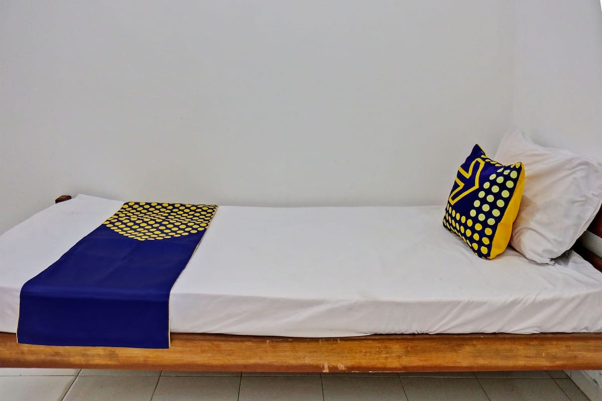 Uma cama de solteiro com lençol branco e manta azul com desenhos amarelos.