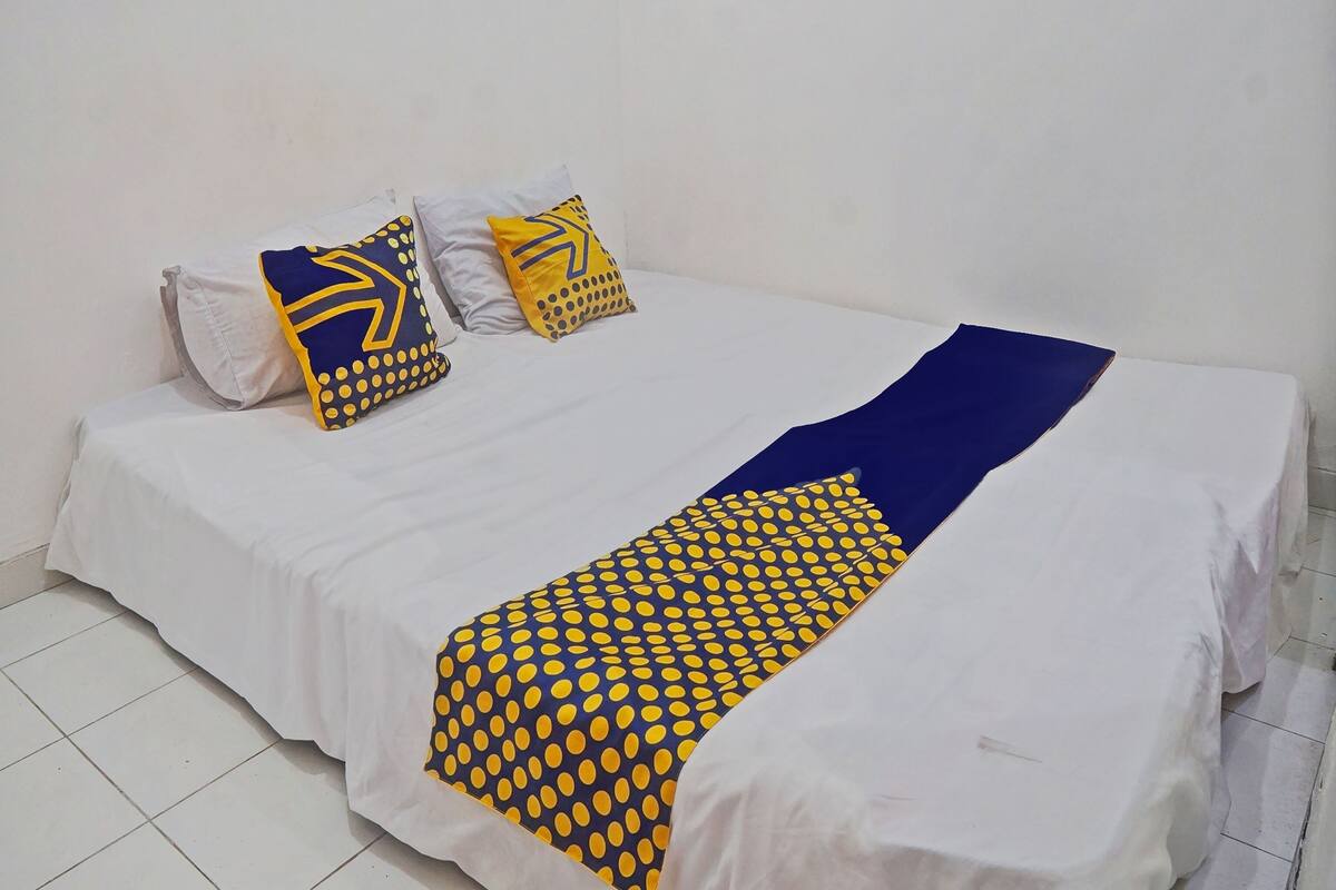 Uma cama com roupa de cama branca, duas almofadas com padrões amarelos e azuis, e um cobertor azul e amarelo.