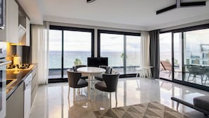 Quarto de hotel moderno com cozinha, área de refeições e grandes janelas com vista para o mar.