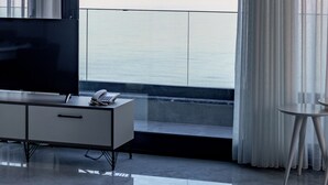 Quarto de hotel moderno com uma grande janela que oferece vista para o mar e montanhas ao longe.