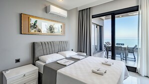 Quarto de hotel moderno com uma cama grande, mesa de cabeceira, guarda-roupa e varanda com vista para o mar.