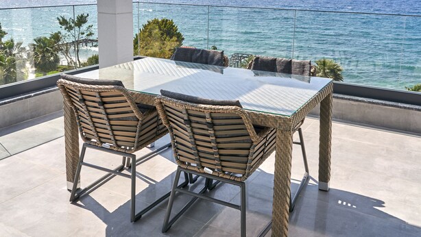 Terraço com mesa de vidro e cadeiras de vime, com vista para o litoral.