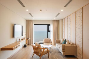 Uma sala de estar moderna com televisão de tela plana, móveis de madeira, um sofá e vista para o mar.