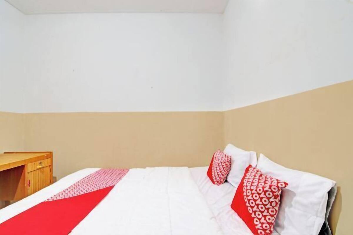 Quarto com cama, escrivaninha de madeira e almofada estampada em vermelho e branco.