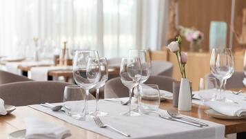 Uma área de refeições com mesas postas para uma refeição, incluindo taças de vinho, pratos e talheres.